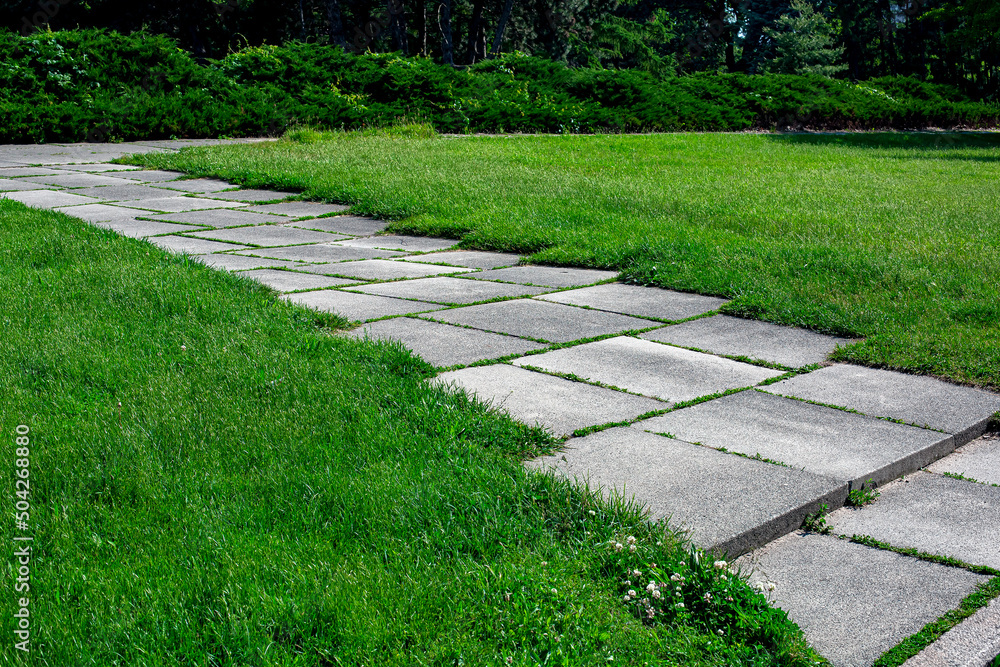 Foto de garden path made of square tiles overgrown with grass in a park ...