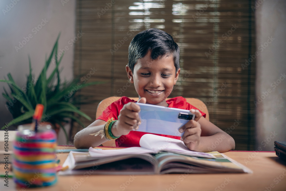 Asian kid using mobile phone while doing homework Stock Photo | Adobe Stock