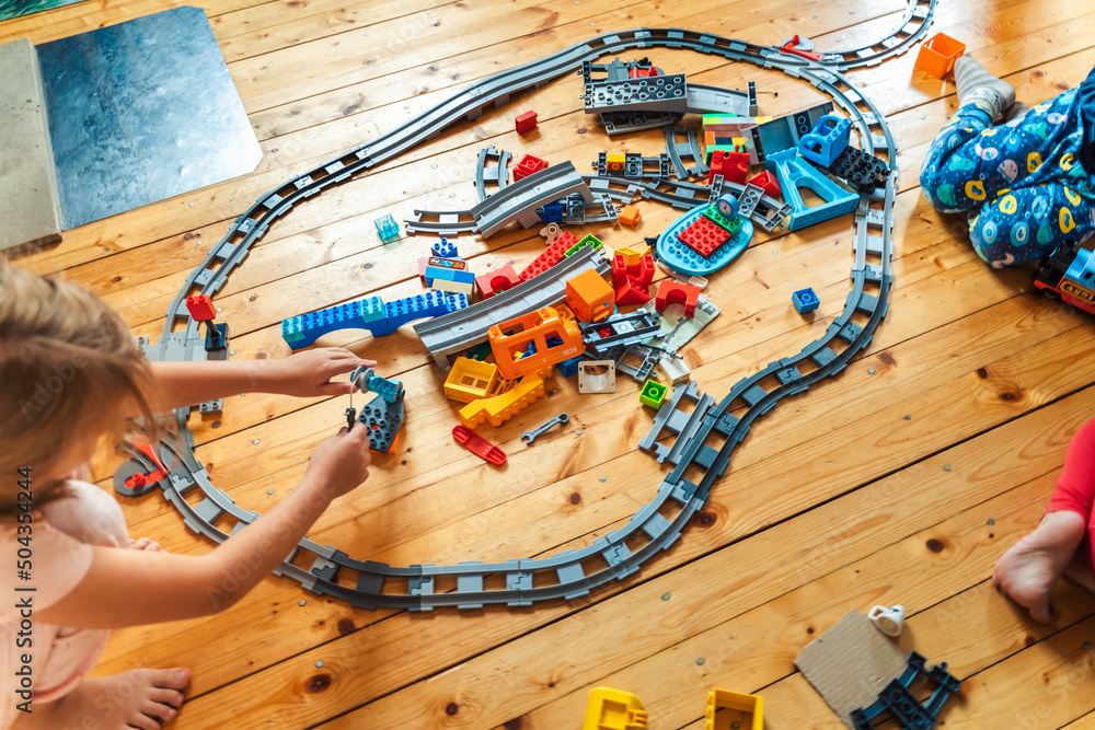 Girls, sisters play kids constructor, build toy railway, railroad by ...