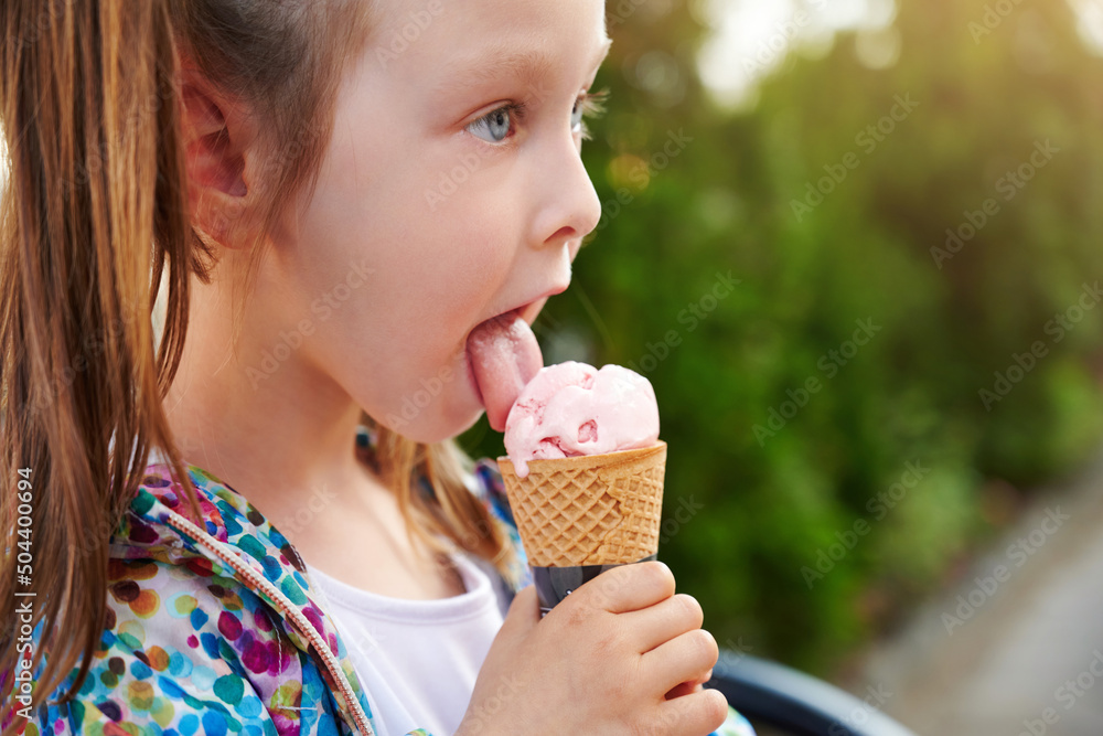 Cheerful kid girl with ice cream in waffle cone is eating licking tongue ice cream. Close-up ice ...