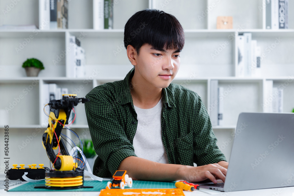 Asian teenager constructing robot arm homework project with laptop in ...