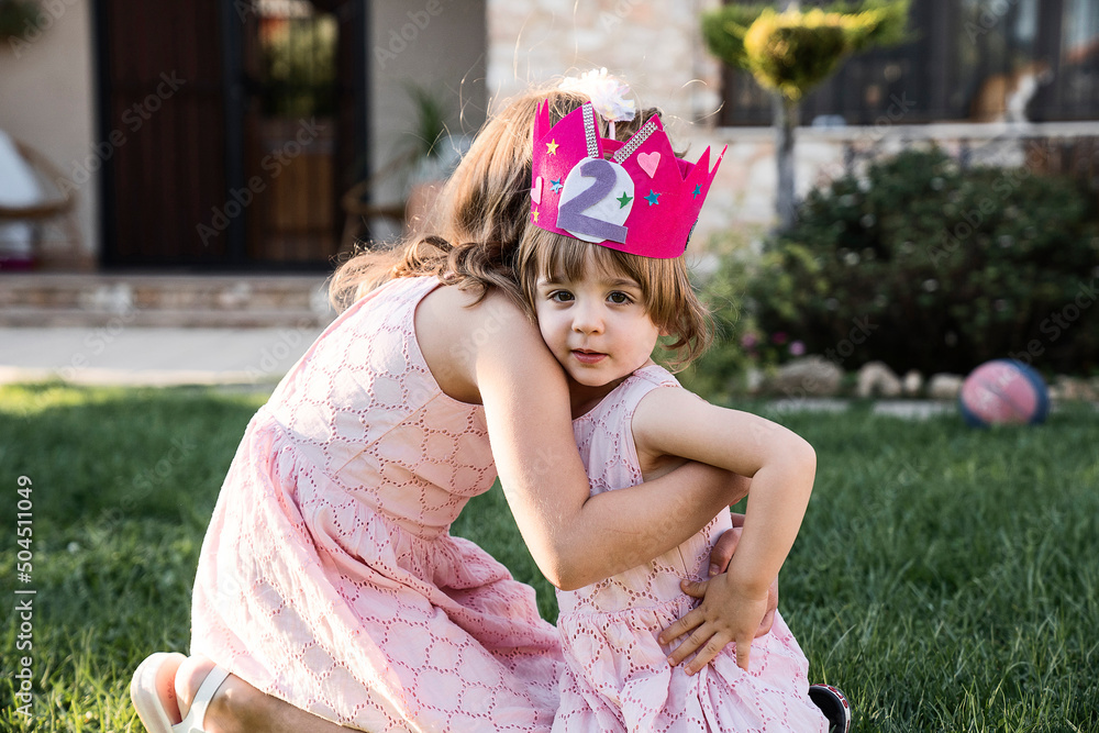 Girls in identical dresses hugging on grass Stock Photo | Adobe Stock