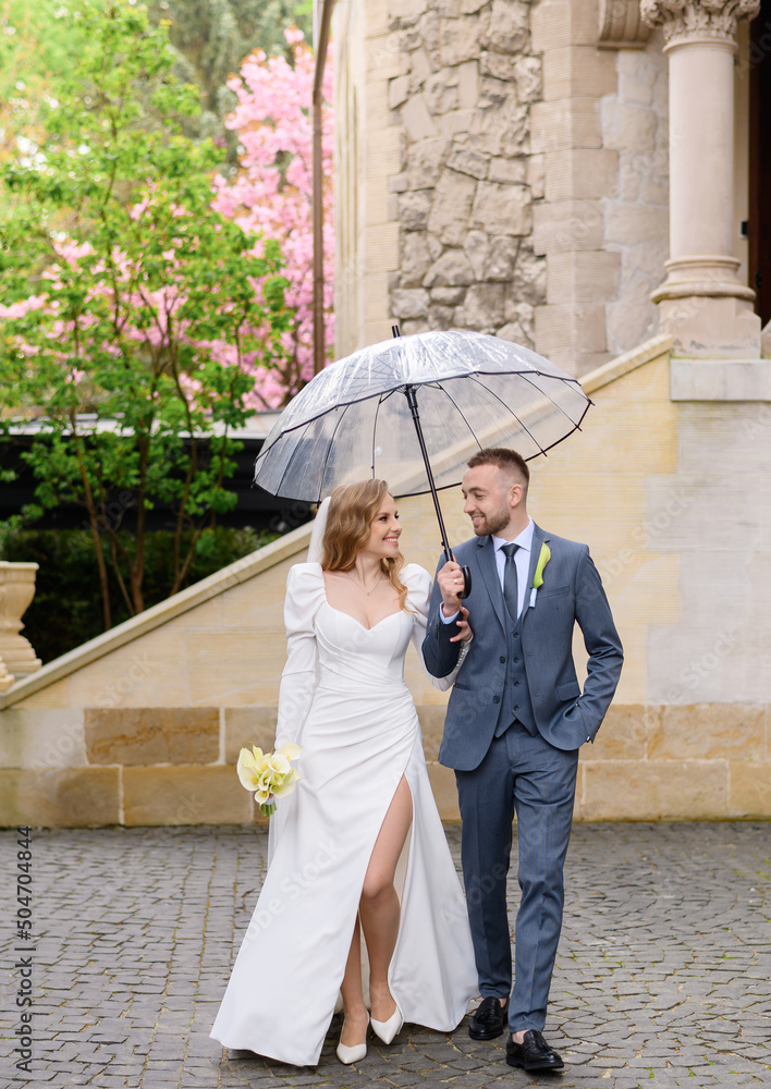 Beautiful caucasian newlywed couple with transparent umbrella poses and ...