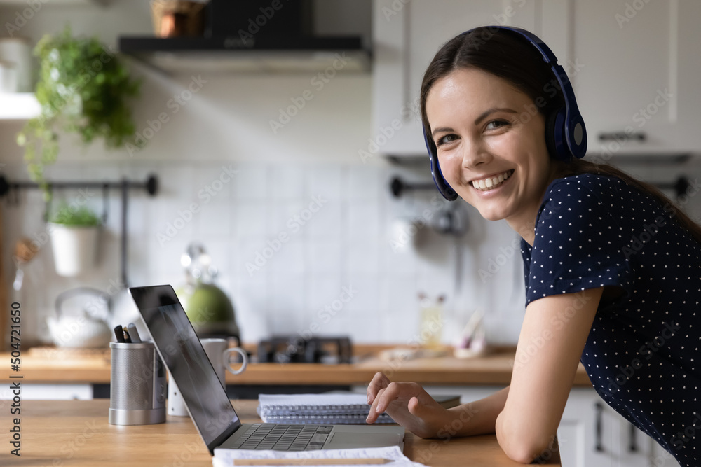 Happy online student in wireless earphones home head shot portrait. Cheerful gen Z girl standing ...