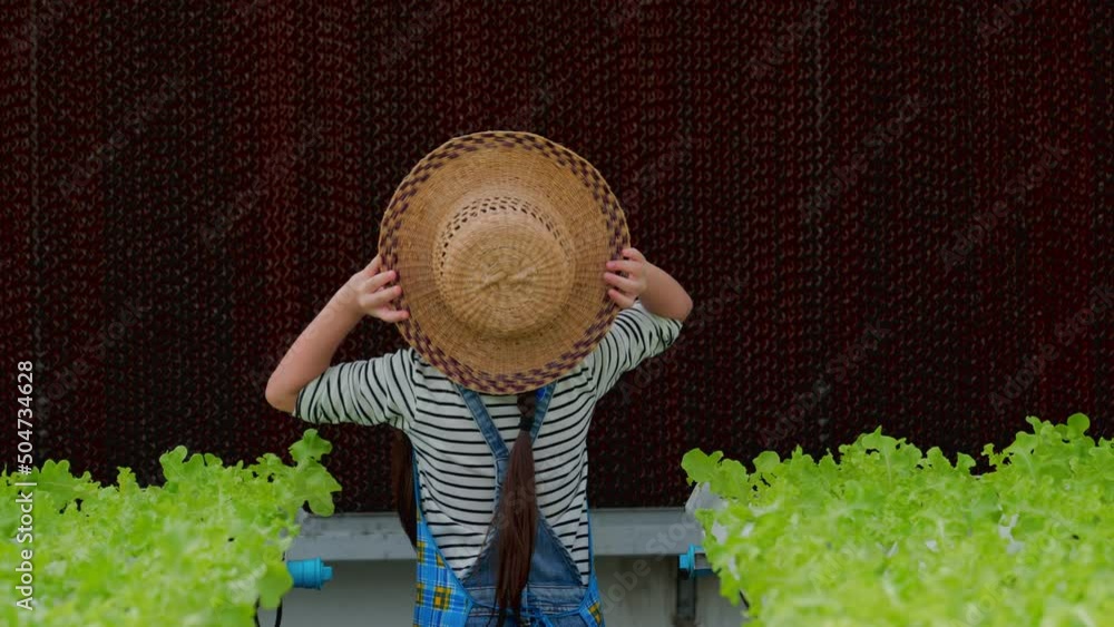 A young girl in a straw hat walks happily in an organic vegetable farm ...
