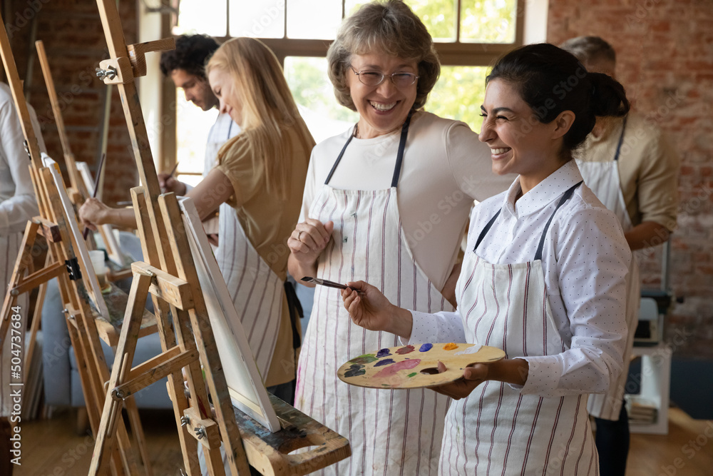 Art school student and older teacher laugh during painting lesson ...