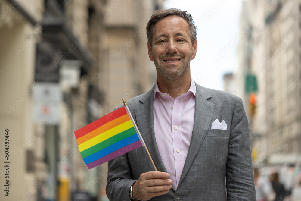 LGBTQ gay man standing on a street holding a rainbow flag smiling happy ...
