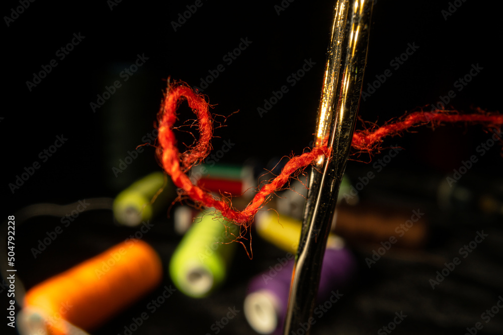 Needle eye threaded with piece of red thread on black background with ...