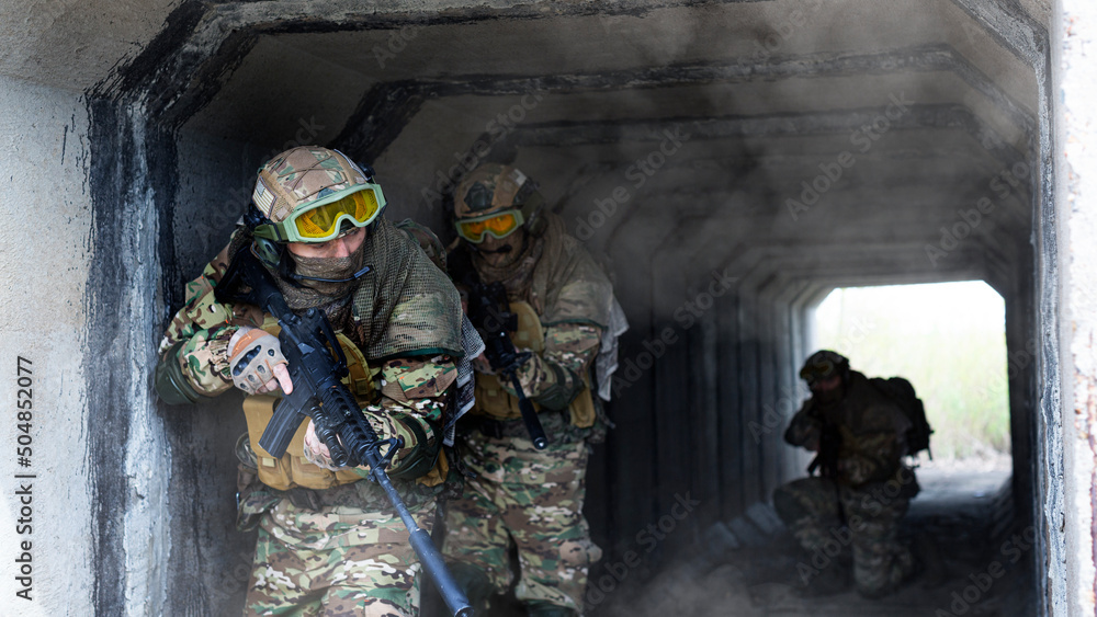Three military mercenaries walk against a concrete wall background and ...