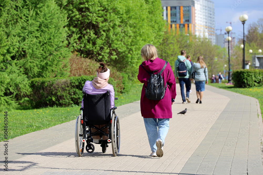 Disabled person in a wheelchair and woman walking on a city street ...