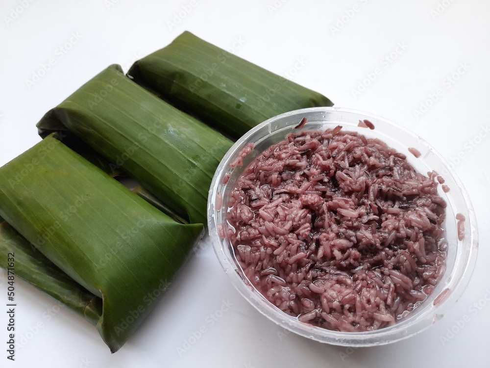 Tape uli wrapped in banana leaves and black sticky rice in a bowl seen ...