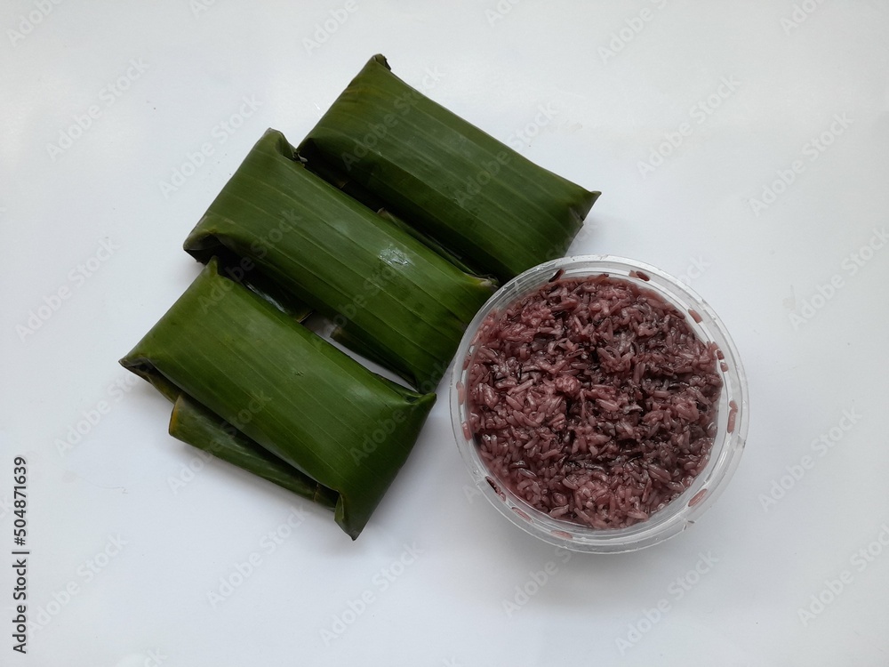 Tape uli wrapped in banana leaves and black sticky rice in a bowl seen ...