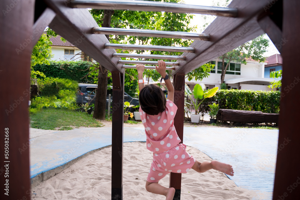 Rear back view. Preschool kid girl is hanging out on bar at playground ...