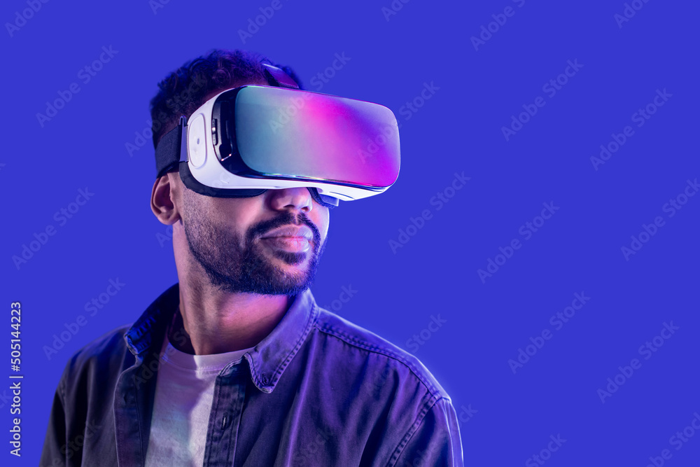 Serious young man using hi tech smart vr glassses isolated on blue ...