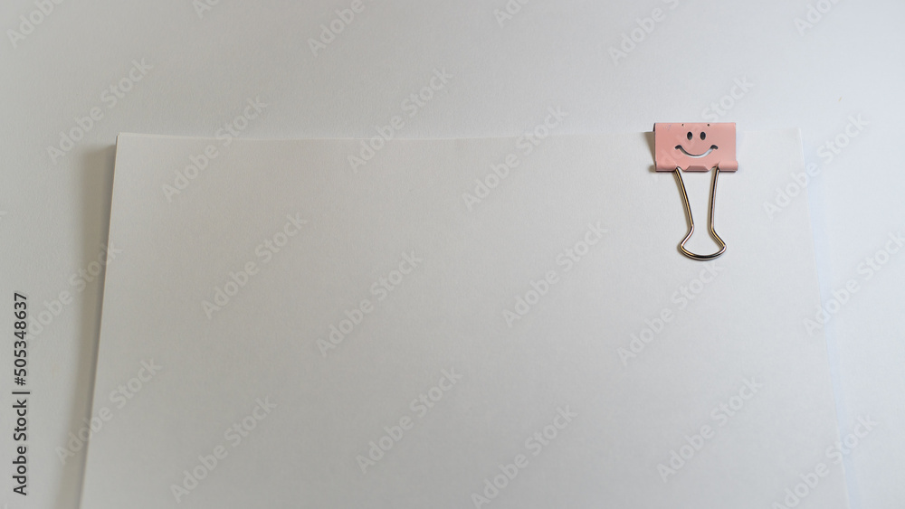a pink metal paperclip with a smiling character attached to a blank ...