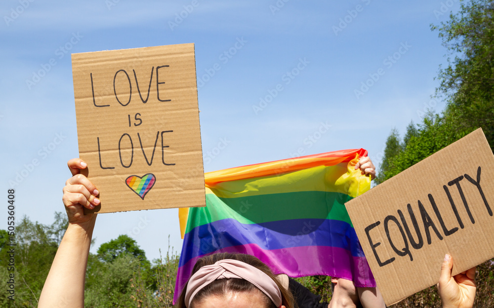 People holding placard signs Love is Love, Equality and a rainbow flag ...