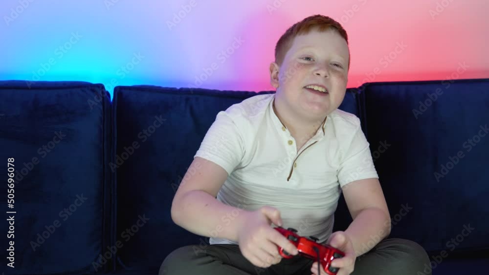 Excited little boy gamer is sitting on a couch, playing and winning in ...