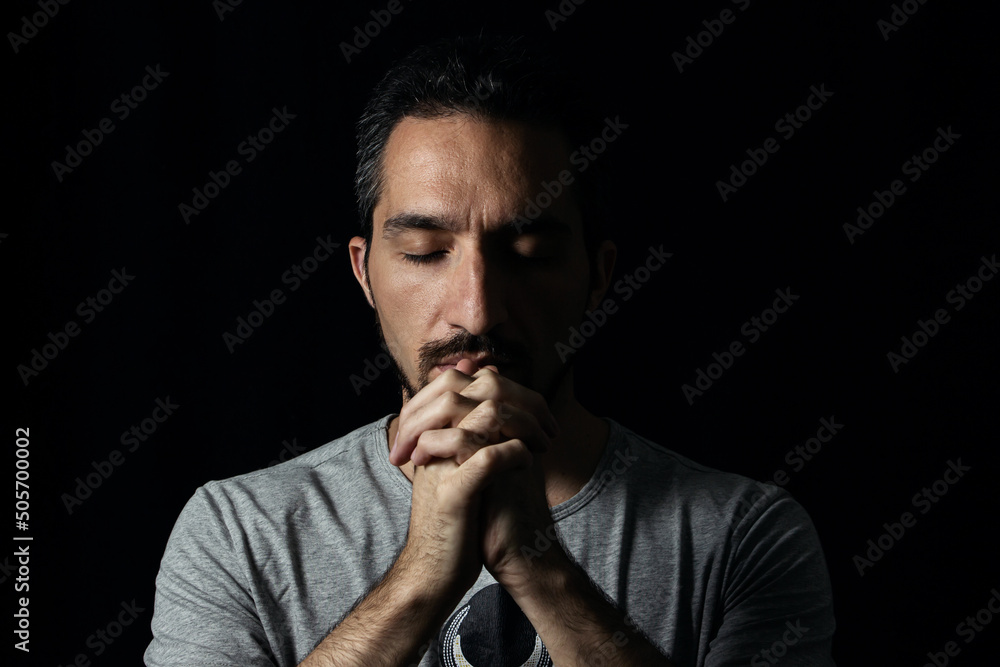 The man folding his hands in prayer to god on a black background ...