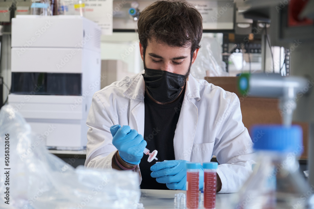 Scientist in white lab coat and protective face mask filter sample into ...