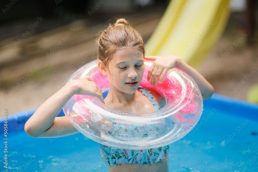 European preteen girl in swimsuit swims on circle in pool in backyard ...