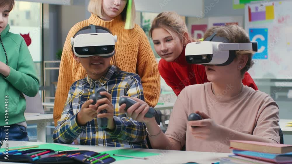 Teenagers looking at classmates in vr headset and joystick playing game ...