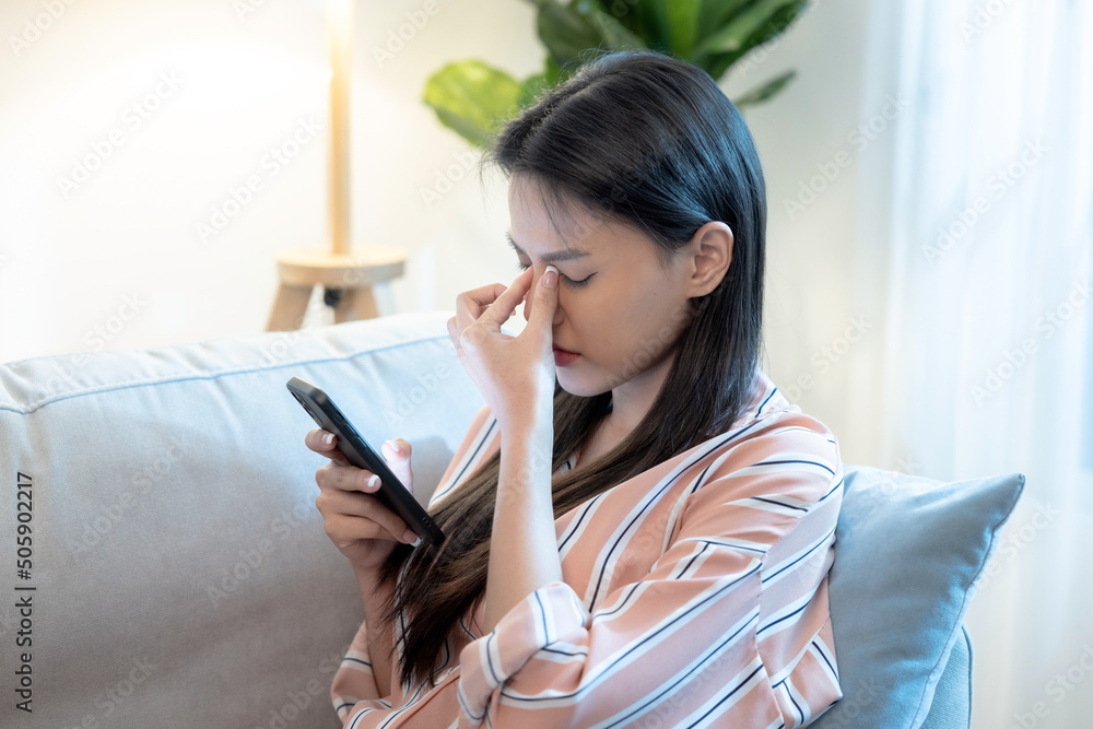 Tired Asian woman suffering eyestrain using mobile phone, Blue light is ...