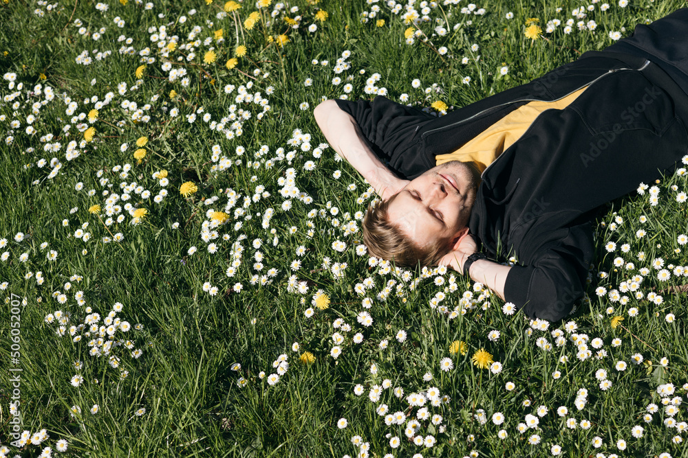Young man laying in green grass with flowers. People fatigue from work ...