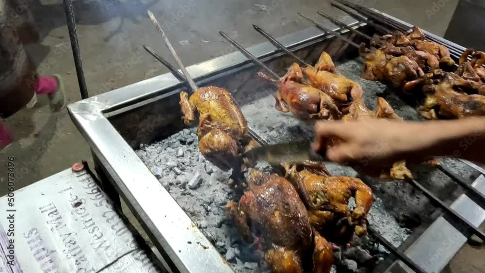 Chicken roasted on spit being grilled over the bright glowing beech ...