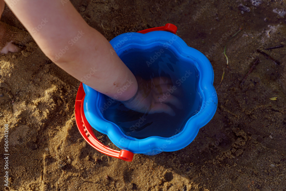 little girl dips her hands in a blue plastic bucket of water on the ...