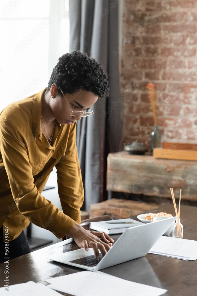 Foto de Vertical view thoughtful African woman lean over desk working ...
