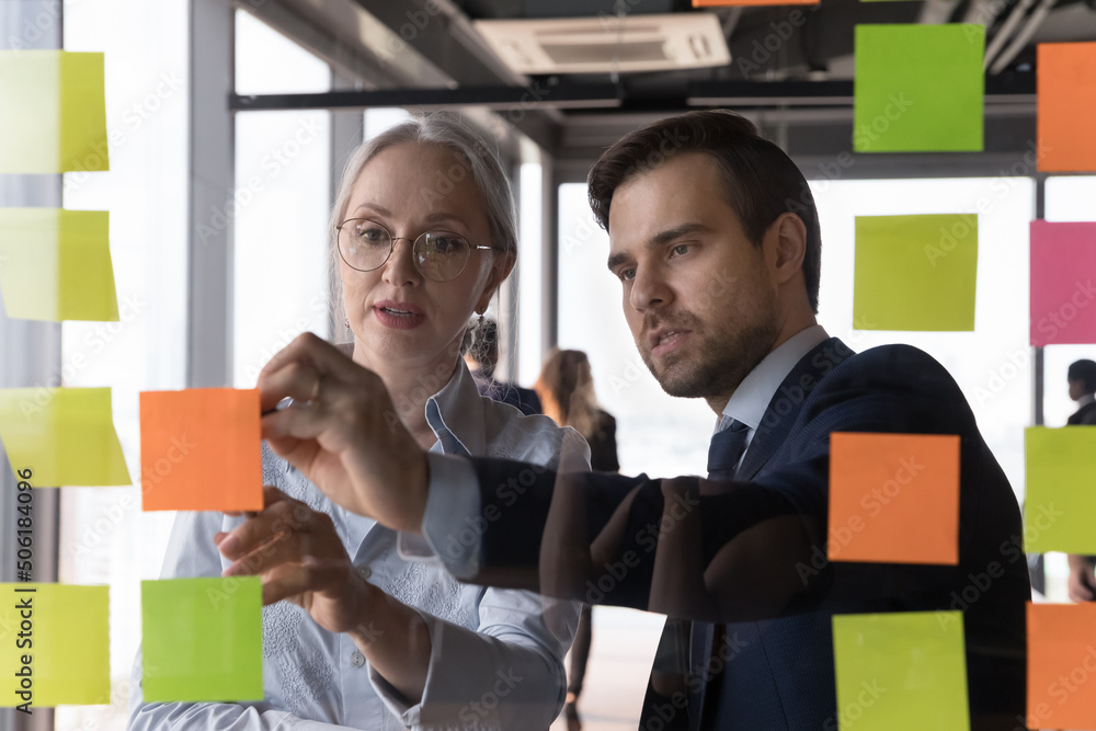 Serious aged and young colleagues analyze corporate goals, discuss ...