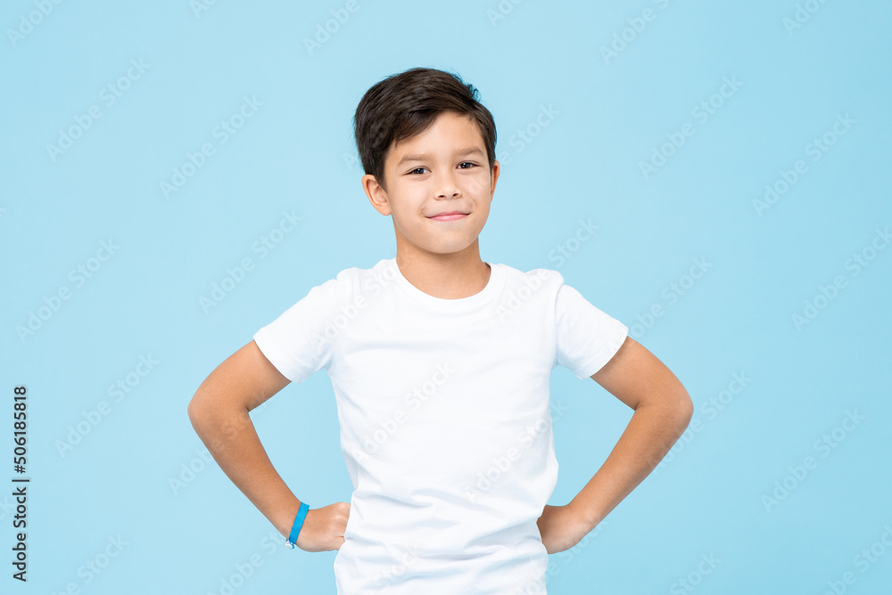 Cute mixed race boy smiling with arms akimbo in studio isolated light ...