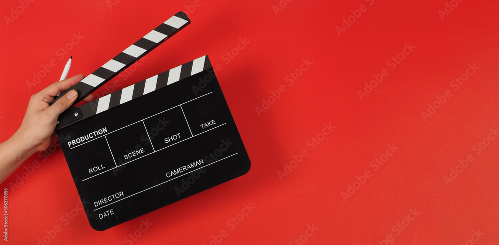 Hand is holding black clapper board with Marker Pen on red background ...