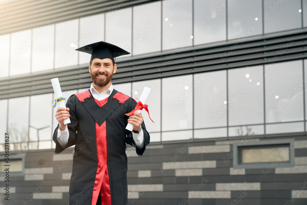Front view of student with master degree standing, holding two diplomas ...