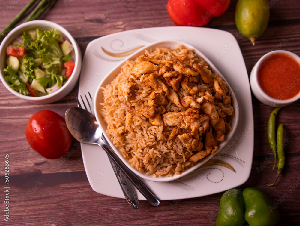 Spicy Indian chicken pulao with salad, sauce and spoon in a dish top ...