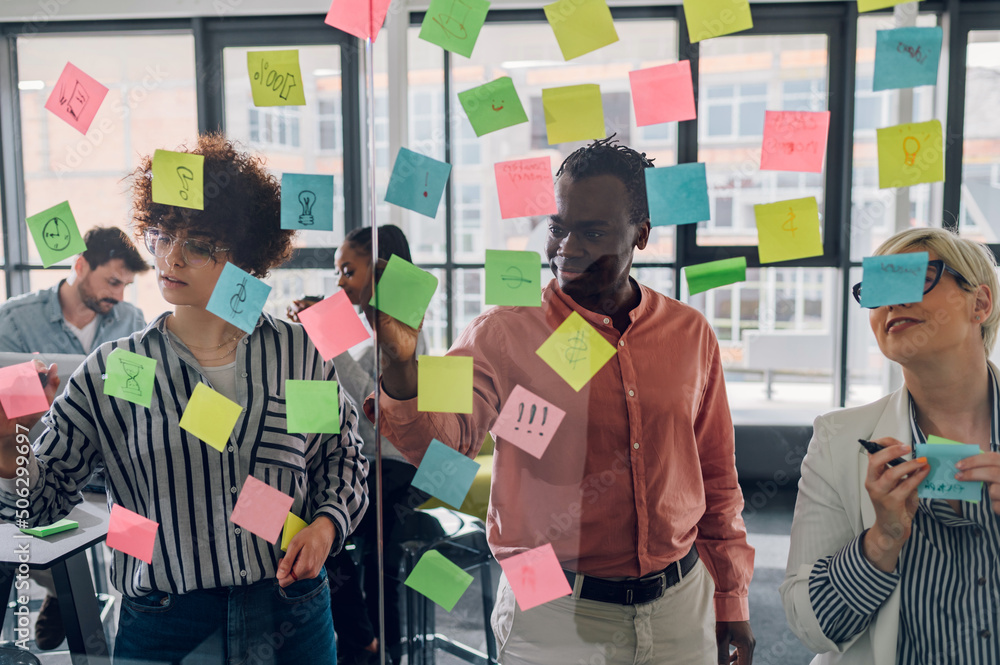 Multiracial team at work writing ideas on sticky notes on the glass ...