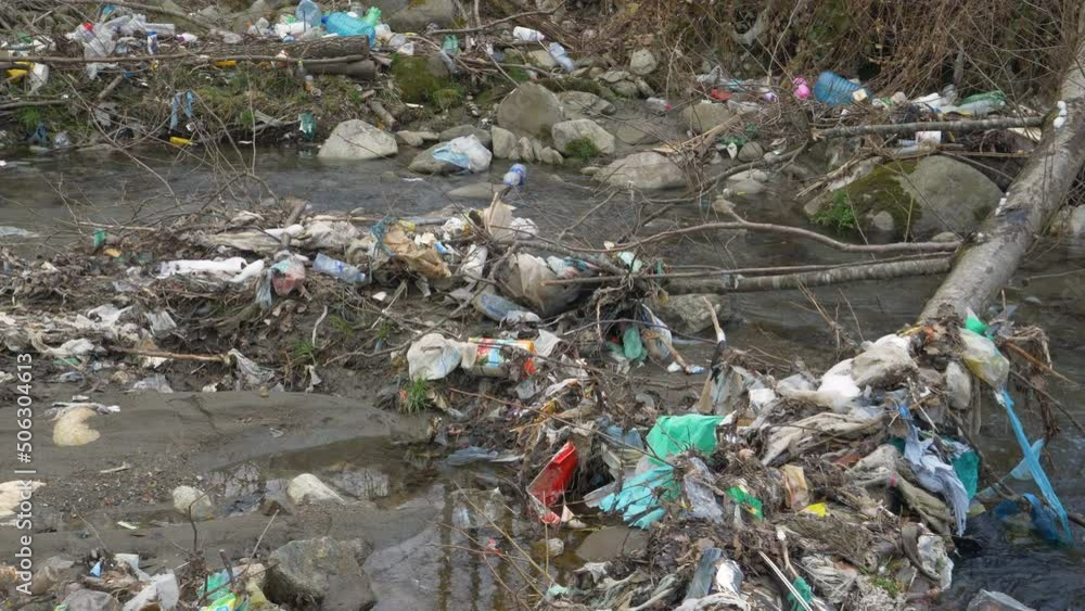 PANNING: View of flowing river surrounded with numerous plastic garbage ...
