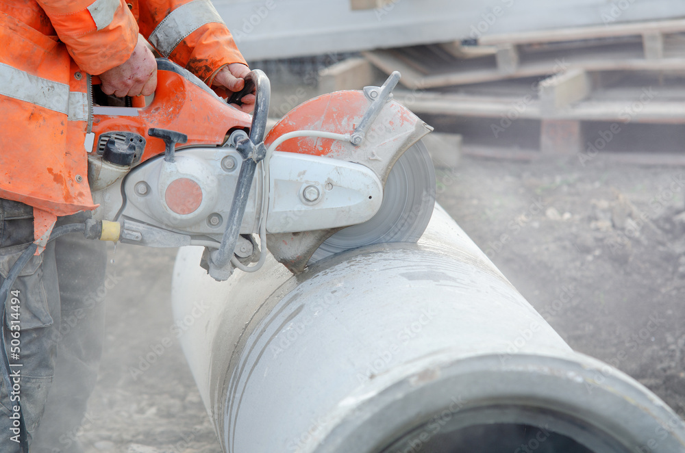 A worker at the construction site cutting a concrete drainage pipe with ...