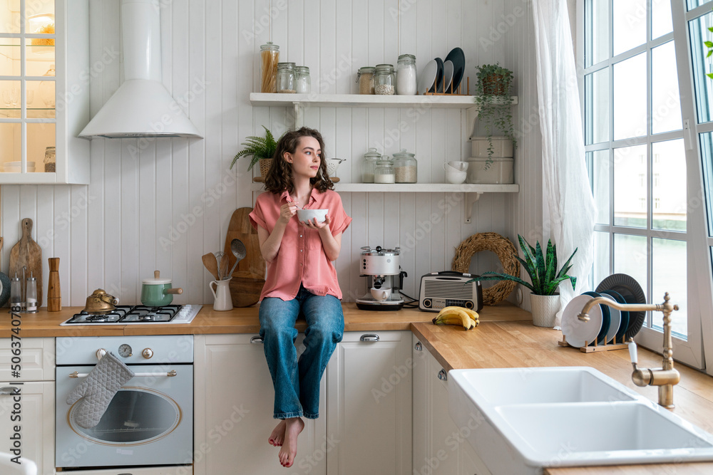 Woman with bowl sitting on kitchen counter at home Stock Photo | Adobe ...