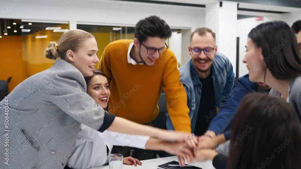 Business people stack hands in pile over meeting table, cheer together ...