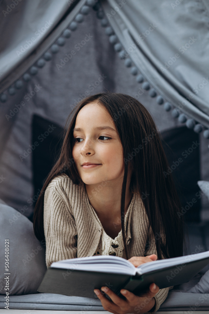 Little girl reading book lying in vigvam Stock Photo | Adobe Stock
