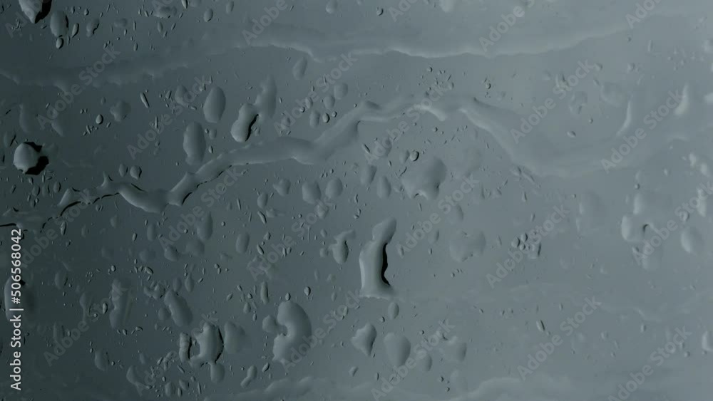 Raindrops run down the glass of the window against the black clouds of ...