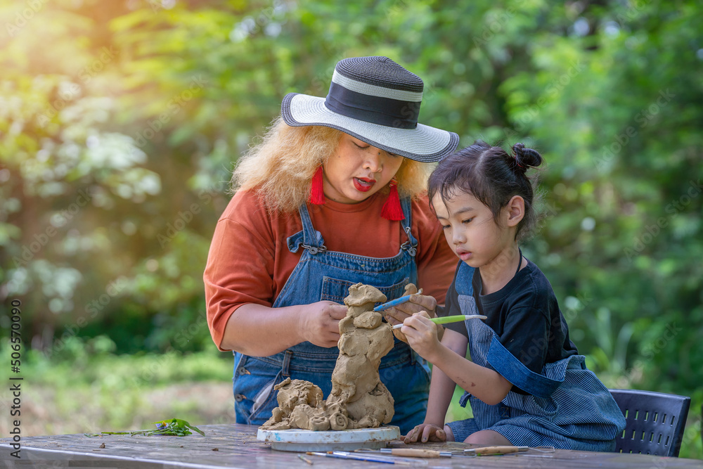 Portrait of little girl and teacher working with pottery clay together ...