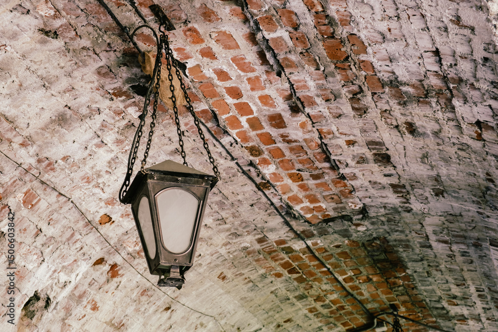 Metal antique lantern on chains hangs from a brick ceiling. Lighting in ...