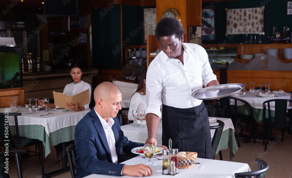 positive male waiter serving order to adult man in restaurante Stock ...