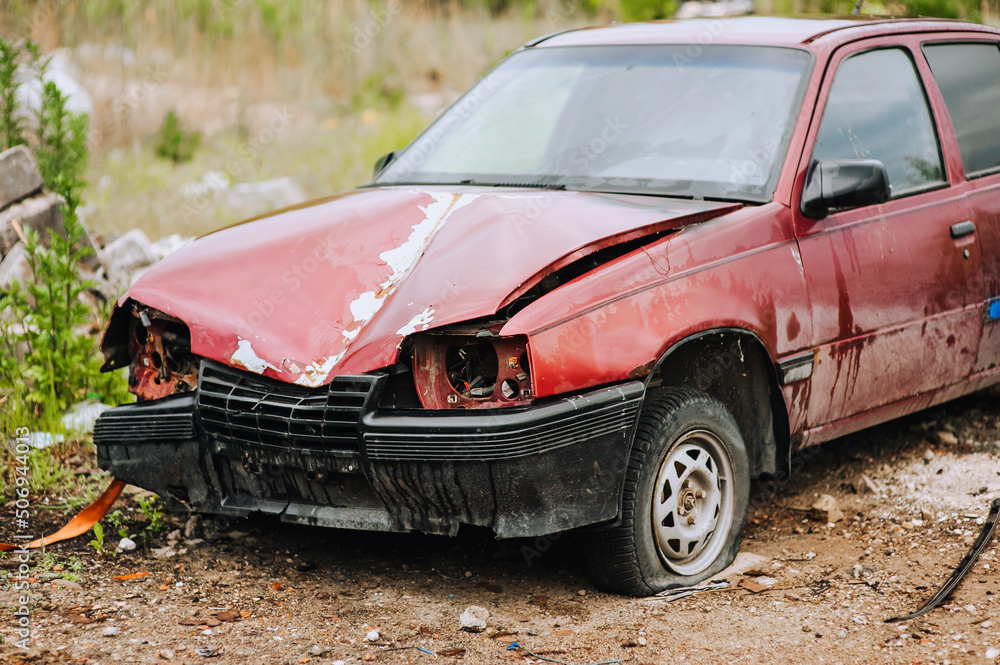 An old, red, broken, discarded car stands in a landfill after the war ...
