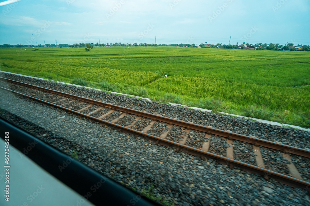 The view of the tracks and rice fields outside the window of the train ...