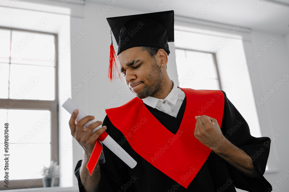 A Black student in graduate gown and square cap who is happy to finish ...