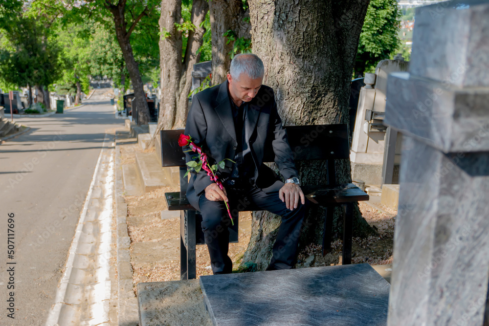 Mature man in black clothes on cemetery, holding a flower and mourning ...