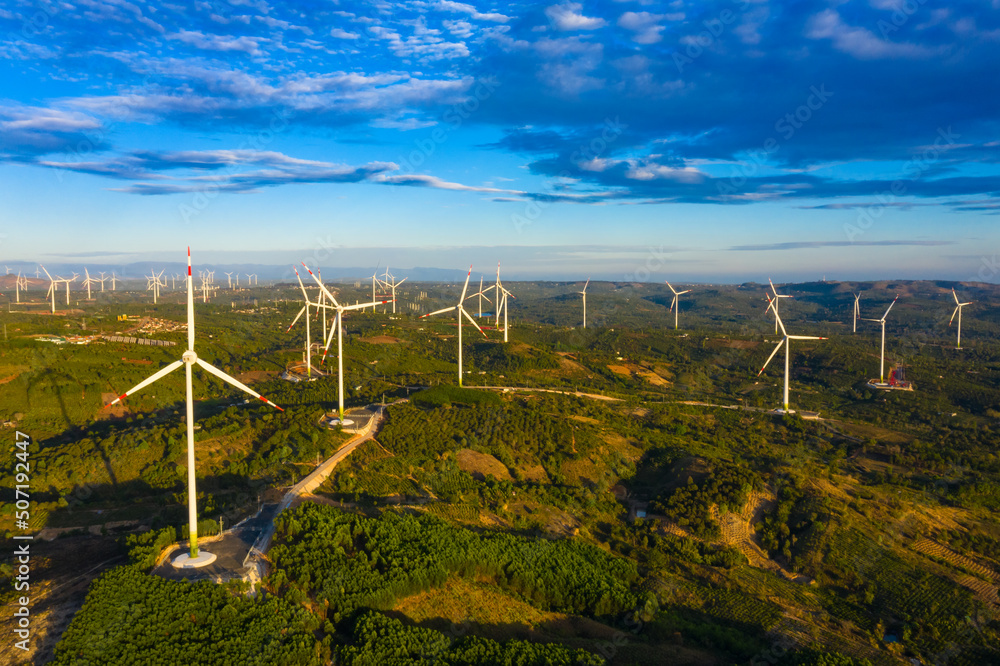 Wind turbines farm in a big green field under the blue sky generating ...